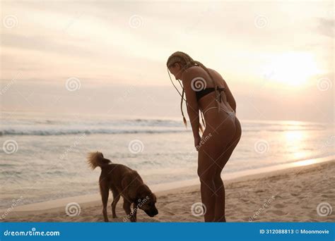 A Young Woman In A Bikini With Braids On The Beach At Sunset Walks With