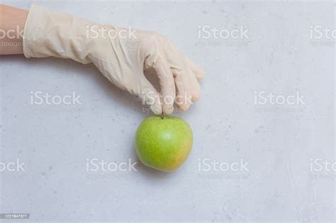고무 장갑을 낀 손에는 녹색 사과 열매가 있습니다 녹색 사과는 밝은 회색과 흰색 현대 콘크리트 배경에 흰색 일회용 고무 라텍스