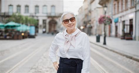 우아한 의상과 트렌디한 선글라스를 쓴 성인 백발의 여성이 야외에서 포즈를 취하고 웃고 있다 배경에 도시 거리입니다 행복한 연금 수급자 사진 Unsplash의