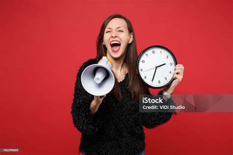 검은 모피 스웨터에 젊은 여자를 웃 고 스튜디오에서 밝은 빨간색 벽 배경에 고립 된 라운드 시계를 들고 확성기에 비명 사람들은 진심으로 감정 라이프 스타일 개념입니다 복사
