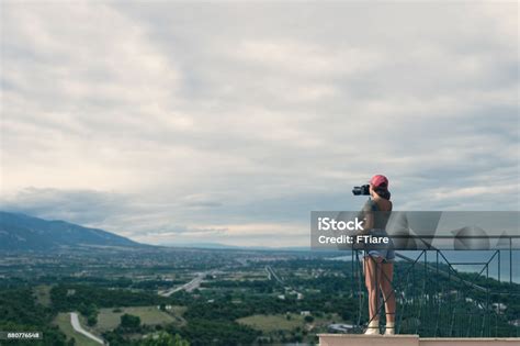 여성 사진 작가 카메라와 함께 빨간 모자에 일몰에 Katerini의 그리스 도시의 맞은편 발코니에 서 있다 Katerini 그리스입니다 보기는 Katerini에 산에서