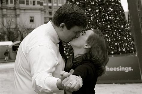 A Man And Woman Are Kissing In Front Of A Christmas Tree With Lights On It