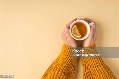 카피 스페이스와 고립 된 파스텔 오렌지 배경에 레몬 슬라이스와 차의 흰색 컵을 들고 노란색 스웨터에 여성의 손의 1 인칭 최고 보기 사진 레저 활동에 대한 스톡 사진 및