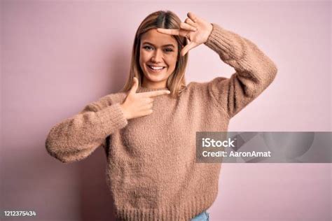 젊은 아름 다운 금발 여자 핑크 고립 된 배경 행복 한 얼굴으로 손과 손가락으로 프레임을 만드는 미소 위에 겨울 울 스웨터를 입고 창의력과 사진 개념 손에 대한 스톡 사진