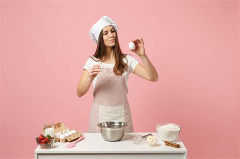 여자 요리사 요리사 또는 제빵에 앞치마 흰색 T 셔츠 모자 요리사 모자 요리 케이크 또는 테이블에 있는 컵 케이크를 유지 계란