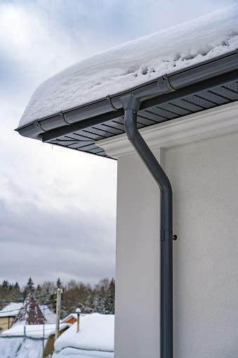 금속 다운 파이프 시스템 거터링 시스템 눈 아래 외부 하강 파이프 및 배수 파이프 회색 금속 타일로 만든 지붕과 겨울에 눈의 두꺼운 층으로 덮여 배수로와 집의 모서리 0명에