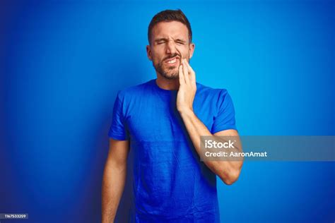 치통이나 치아 질환으로 인해 고통스러운 표정으로 입을 만지는 파란색 고립 된 배경 위에 캐주얼 한 티셔츠를 입은 젊은 잘생긴 남자 치과 의사 개념 T 셔츠에 대한 스톡 사진