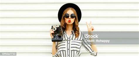 검은 둥근 모자를 쓰고 입술을 불고있는 필름 카메라 흰색 배경에 줄무늬 셔츠 광고 텍스트를위한 배너 빈 복사 공간을 가진 행복한 젊은 여성 사진 작가의 초상화 모자 모자류에