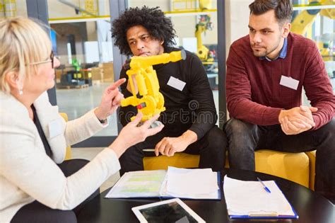 Team Discussing Robotics Development And Automation With A Gripper Arm Model In Office Setting