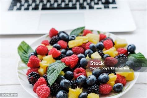 노트북과 무지개 색상 파인애플 딸기 블루베리와 라스베리 흰색 테이블에 민트에서 건강 한 열매와 함께 작업 영역 건강한 식생활에