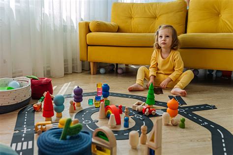 아이는 장난감 마을과 자동차 트랙을 만듭니다 바닥에 앉아있는 어린 소녀는 놀이방에서 장난감 무지개 블록 자동차 및 도로를 가지고 놀고 있습니다 현대 보육원에서 아기와 유아를