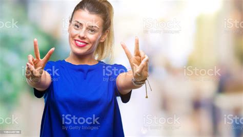 손가락 하 고 승리 기호를 보여주는 카메라를 보고 웃 고 고립 된 배경 위에 캐주얼 블루 티셔츠를 입고 젊은 아름 다운 여자