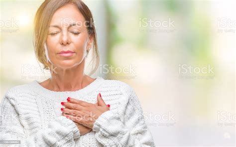 격리 된 배경으로 미소를 통해 중 년 수석 히스패닉 여자 입고 겨울 스웨터 닫힌된 눈과 얼굴에 감사 제스처와 함께 가슴에 손 건강 개념입니다 겨울에 대한 스톡 사진 및 기타