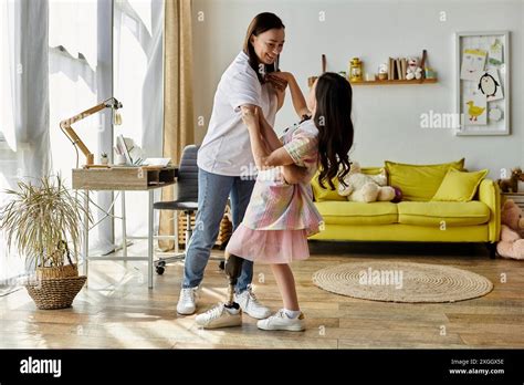 A Brunette Mother And Her Daughter With A Prosthetic Leg Are Dancing Together At Home Stock