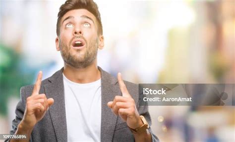 격리 된 배경 위에 젊은 잘생긴 사업가 깜짝 놀라게 하 고 올려 고 손가락으로 가리키는 놀라게 하 고 무기를 제기 가리키기에 대한 스톡 사진 및 기타 이미지 Istock
