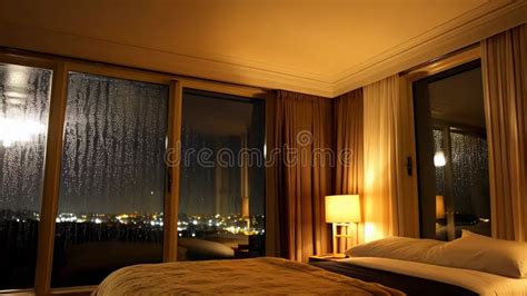 Warm Hotel Bedroom With Night City View And Raindrops On Large Glass
