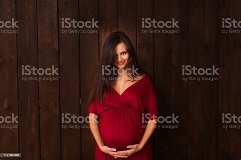 빨간 드레스를 입은 임산부는 어두운 갈색 배경에 배에 손을 들고 있습니다 임신 출산 기대 개념 임신의 아름다운 부드러운 분위기