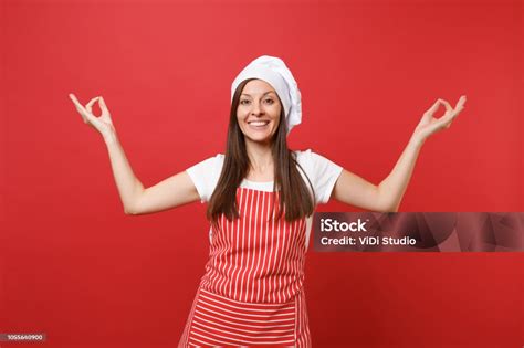 주부 여성 요리사 요리사 또는 줄무늬 앞치마에 베이커 백색 T셔츠 모자 요리사 모자 빨간 벽 배경에 고립 미소가 정부 여자 잡아 요가 제스처에 손 복사 공간 개념을 비웃는