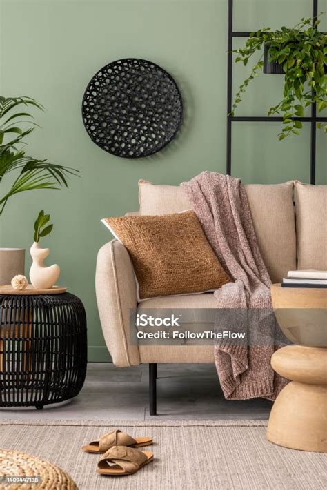 디자인 베이지 색 소파 커피 테이블 식물 및 우아한 개인 액세서리가있는 조화로운 거실 인테리어의 인테리어 디자인 갈색 베개와