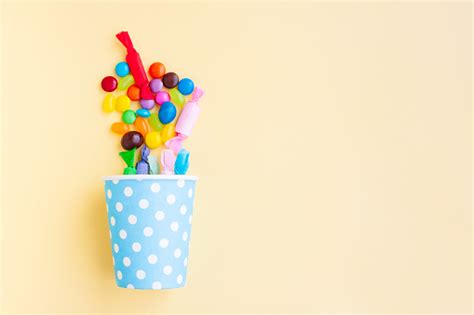 노란색 배경에 하얀 점이 있는 파란 종이컵에서 나온 다양한 종류의 다채로운 사탕 다양한 사탕 가리키기에 대한 스톡 사진 및 기타 이미지 Istock