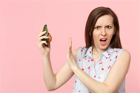 분홍색 파스텔 배경에 고립 된 녹색 아보카도 과일에 손바닥으로 중지 제스처를 보여주는 여름 옷에서 혐오 젊은 여자 사람들은 생생한 라이프 스타일 휴식 휴가 개념입니다 복사