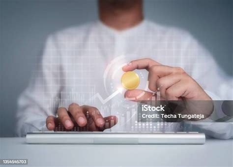 투자 이익 및 비즈니스 성장 개념 흰색 셔츠를 입은 사업가가 흰색 테이블에 키보드 컴퓨터에서 다양한 차트 그래프가 증가하는 상승 화살표로 손으로 황금 동전을 들고 있습니다