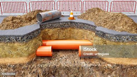 도로 작업 및 지하 파이프 개조의 개념 새로운 오렌지색 Pvc 파이프는 오래된 녹슨 섹션 대신 설치 땅의 조각과 아스팔트에 파고 구덩이 토양의 고분은 도로 원뿔과 울타리와