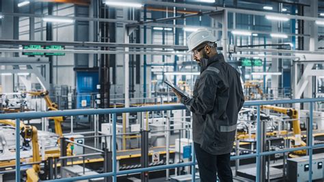 태블릿 컴퓨터를 사용하여 작업 유니폼에 자동차 공장 엔지니어 로봇 무기 기술로 차량 생산에 종사하는 자동차 산업 제조 시설 자동화된 조립 공장 30 34세에 대한 스톡 사진