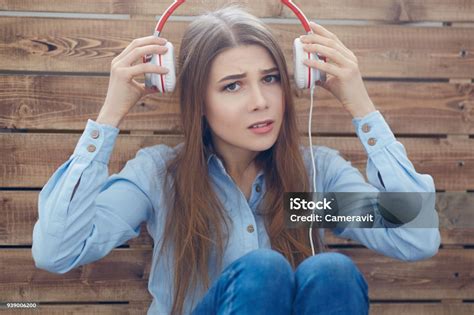 헤드폰으로 젊은 갈색 머리 여자 나무 보드 벽의 배경에 앉아 음악을 듣고 중단 되었습니다 헤드폰에서 소녀 듣는 음악 개념에 대한