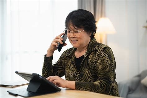 안경을 쓴 중년 여성이 집에서 스마트폰과 태블릿을 사용하고 전화를 걸며 미소 짓고 모던한 인테리어 디자인 원격 근무 65 69세에 대한 스톡 사진 및 기타 이미지 Istock