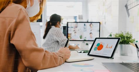 아시아 사업가들은 데스크톱을 사용하여 안면 마스크를 착용하고 뉴 노멀 사무실에서 화상 통화 회의에서 계획에 대해 브레인스토밍하는 동료들과 이야기합니다 코로나 바이러스