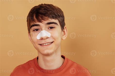 Close Up Portrait Of A Male Teenager Applying A Cleansing Nose Strip To Remove Black Dots