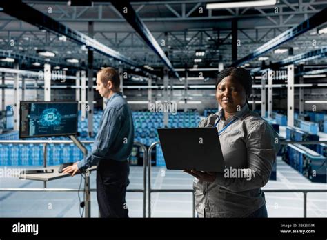Portrait Of Smiling Female Engineer In Server Farm Next To Colleague Doing Infrastructure Ai