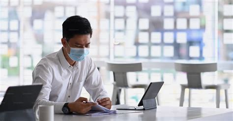 보호 마스크를 쓴 사업가는 태블릿 컴퓨터로 작업하고 사무실 책상에서 비즈니스 데이터를 분석합니다 사진 Unsplash의