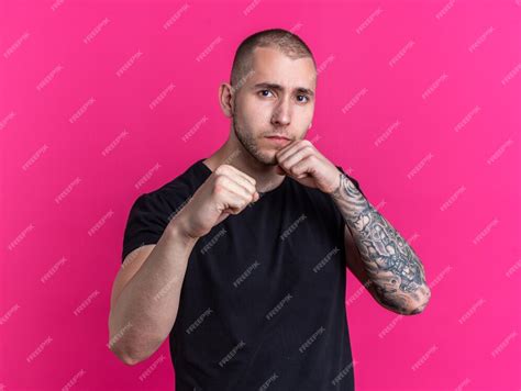 분홍색 배경에 고립 된 포즈 싸움에 검은 티셔츠 서 입고 엄격한 젊은 잘 생긴 남자 무료 사진