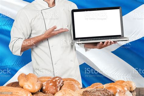 스코틀랜드 국기와 빵 배경에 노트북을 들고 스코틀랜드 베이커 요리사가 복사 공간에 대 한 균일 한 포인팅 빈 화면을 착용 고급 요리에 대한 스톡 사진 및 기타 이미지