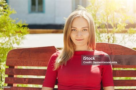 주 근 깨와 여름 날씨와 신선한 공기를 카메라에 즐겁게 보고 감탄 하는 공원에서 벤치에 앉아 빨간 스웨터를 입고 파란 눈 머리 불공평예쁜 젊은 여자의 가로 세로 곧은에 대한