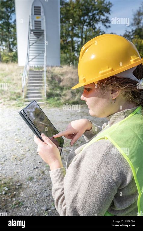 Female Engineer With Brown Curly Hair And Yellow Helmet Is Typing On