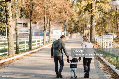 엄마 아빠는 해질녘에 공원을 걷고 있는 아들의 손을 잡고 있다 휴가에 함께 시간을 보내는 가족 어머니 아버지 자연 속의 숲 근처 거리에서 달리는 아이 가을 휴가의 개념입니다