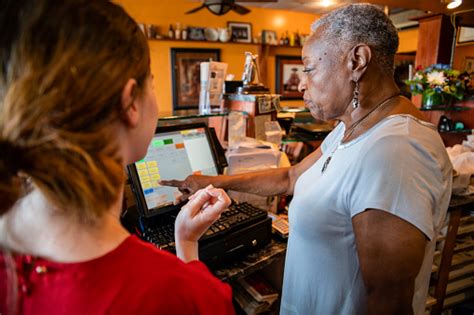 활성 수석 77년오래 된 아프리카계 미국인 사업가 비즈니스 소유자 교육 새로운 직원 18 년 오래 된 백인 백인 여자 작은 현지 식당에서 전산화 금전 등록기를 사용 하는