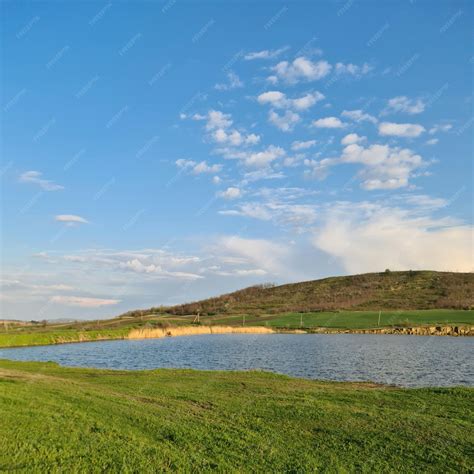 Premium Photo A Grassy Hill With A Small Pond In The Foreground And A