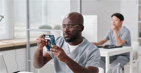 젊은 진지한 수리공이 여성 동료에 대해 직장에서 앉아 있는 동안 손에 전자 장치의 회로 기판을 보고 있다 사진 Unsplash의 사람 이미지