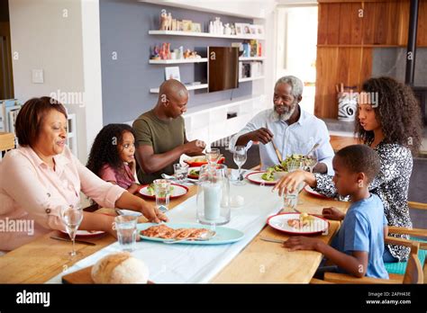 Multi-Generation Family Sitting Around Table At Home Enjoying Meal Together Stock Photo - Alamy