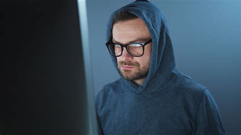 Male Hacker In The Hood And Glasses Working On A Computer In A Dark