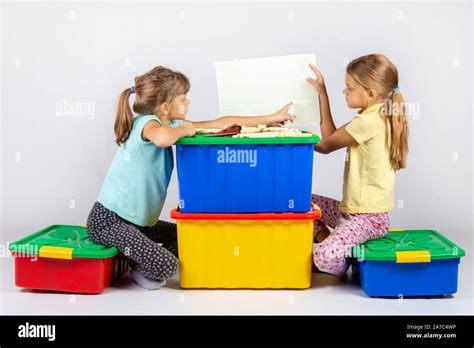 Two Girls Sit On Large Toy Boxes And Look At The Toy Assembly