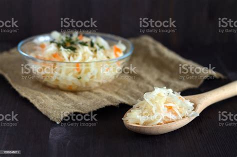 검은 색 배경에 유리 접시에 허브와 당근과 수제 소금에 절인 양배추 나무 테이블에 자루천이 있는 숟가락에 양배추를 절인 양배추 통조림 식품의 개념 복사 공간을 복사합니다