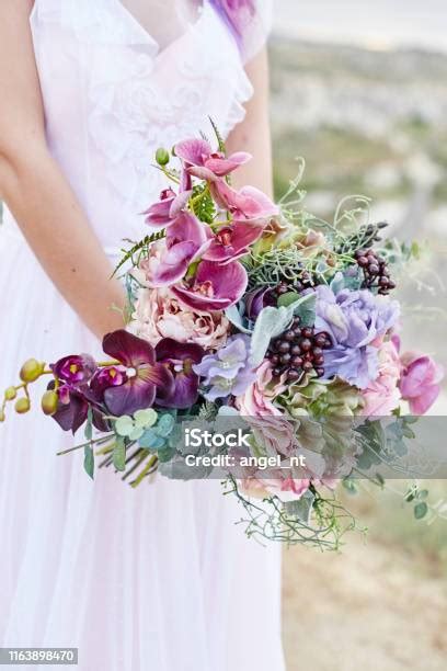 그녀의 손에 꽃의 아름다운 꽃다발을 가진 여자는 새벽 일몰의 광선에 산에 서있다 여자 몸에 아름 다운 흰색 긴 드레스입니다 핑크 머리와 완벽한 신부 결혼식에 대한 스톡 사진