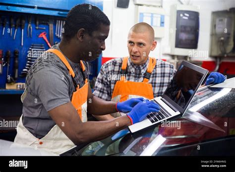 Two auto mechanics diagnosing car engine with laptop Stock Photo - Alamy