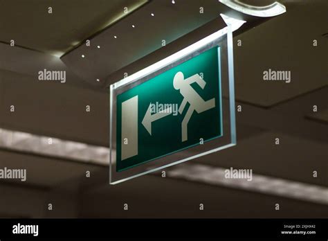 The Image Captures An Illuminated Exit Sign Mounted On The Ceiling The Sign Features A Green