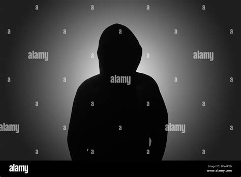 mysterious man wearing black hoodie standing against dark background